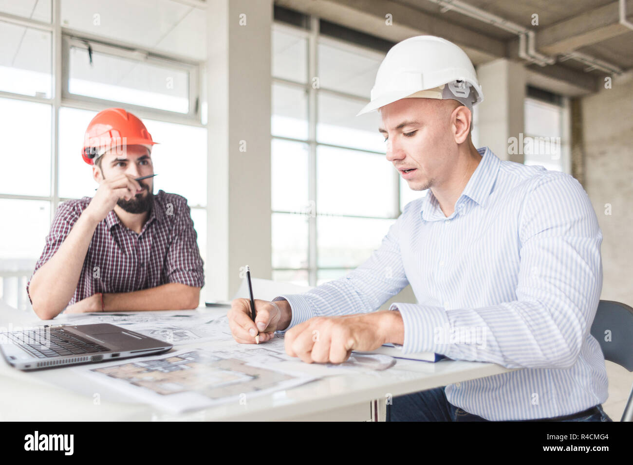 male engineers, architects working at the desk in helmets. Drawings ...