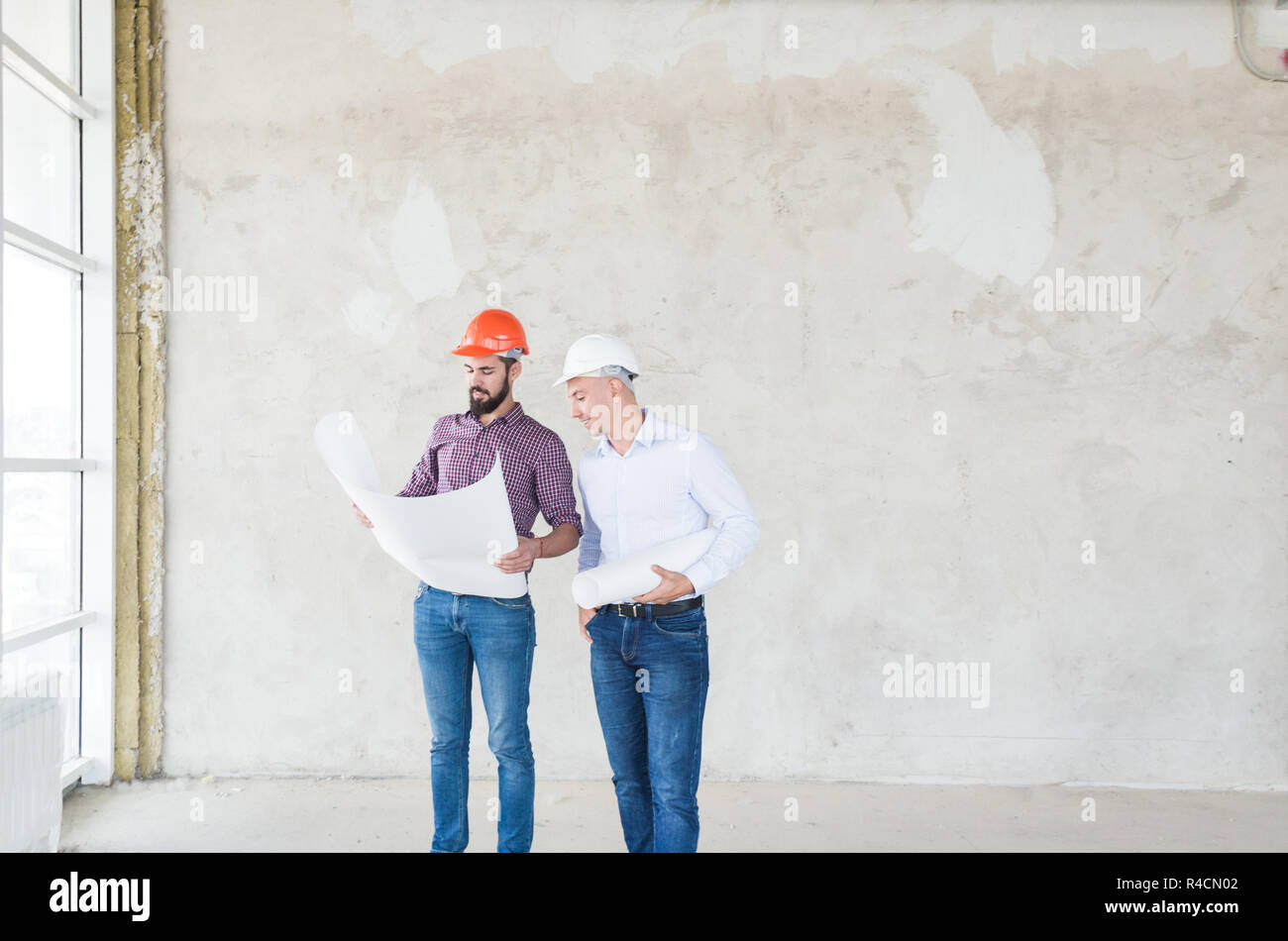 male engineers, architects in helmets stand by the window and hold a ...
