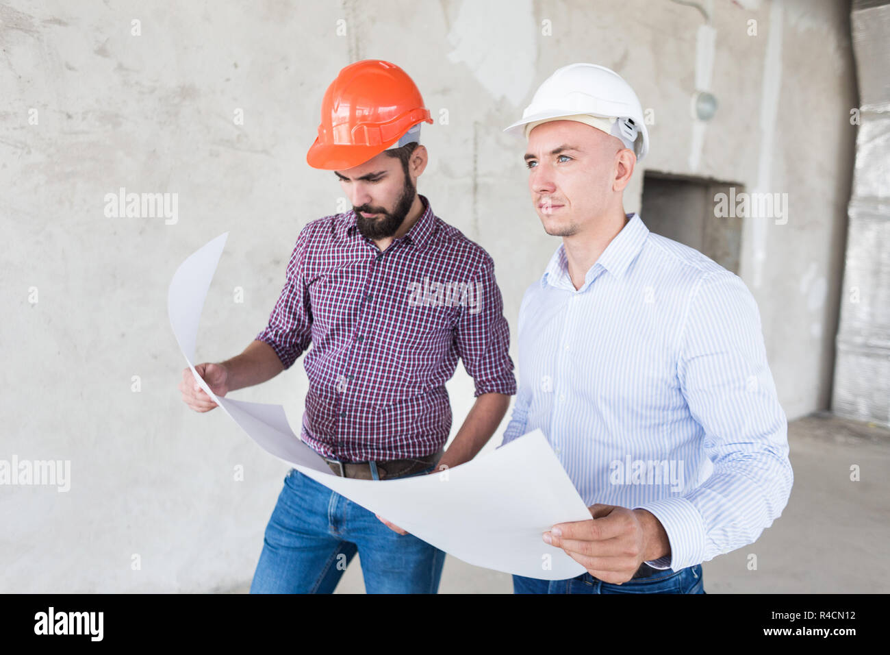 male engineers, architects in helmets stand by the window and hold a ...
