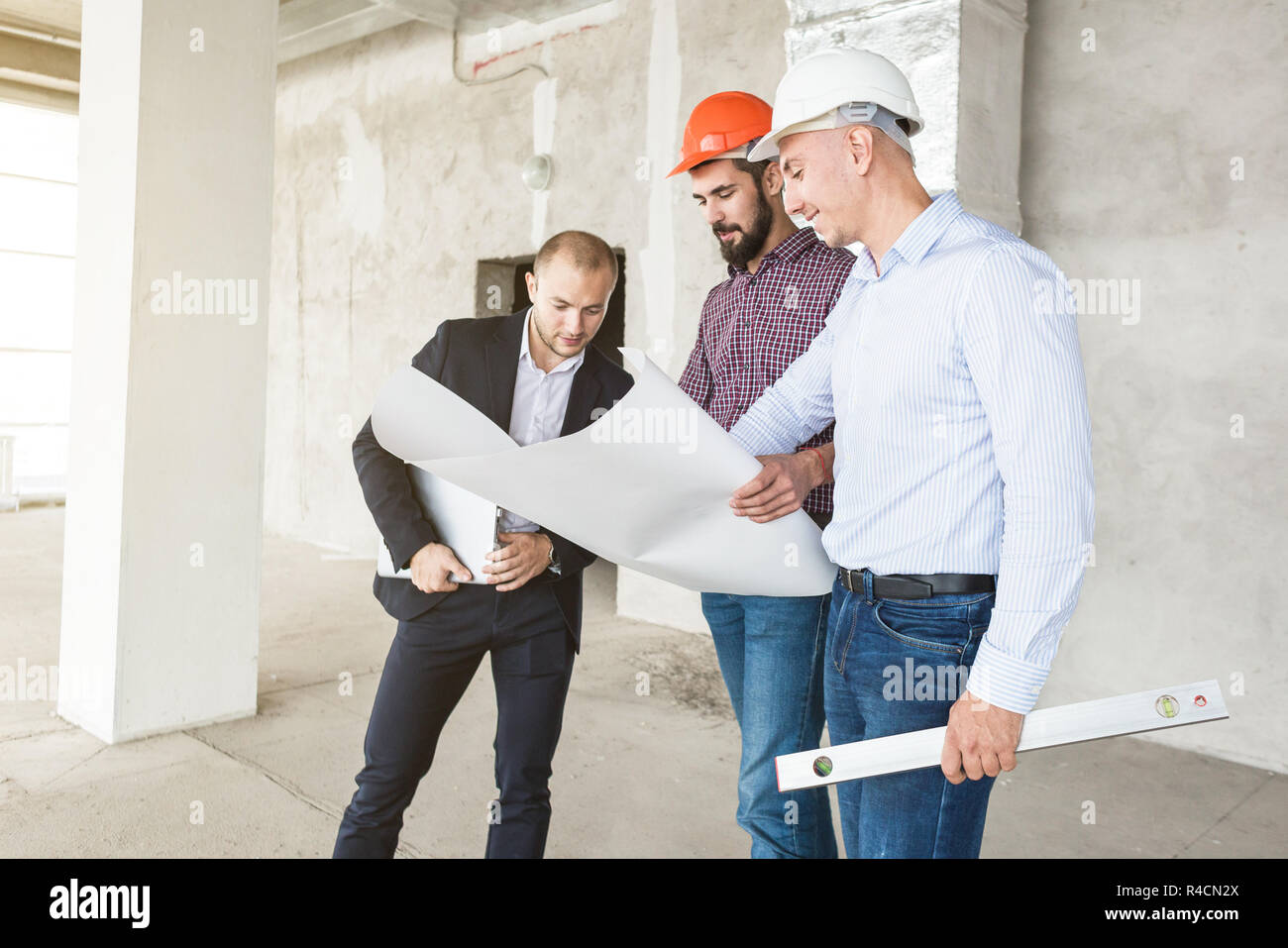 male engineers, architects in helmets stand by the window and hold a ...