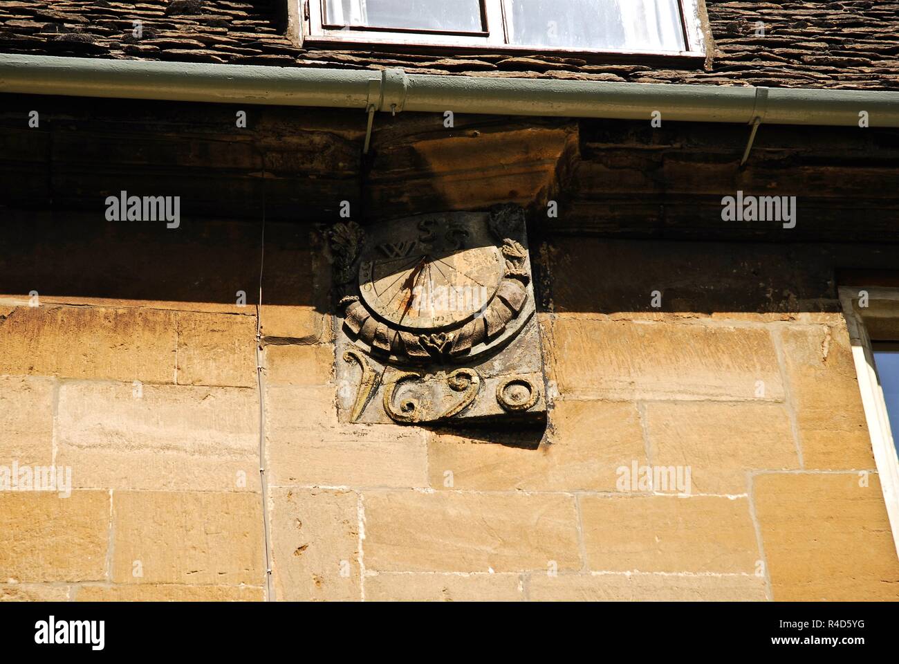 Wall mounted carved sun dial on the wall of a Cotswold stone building ...