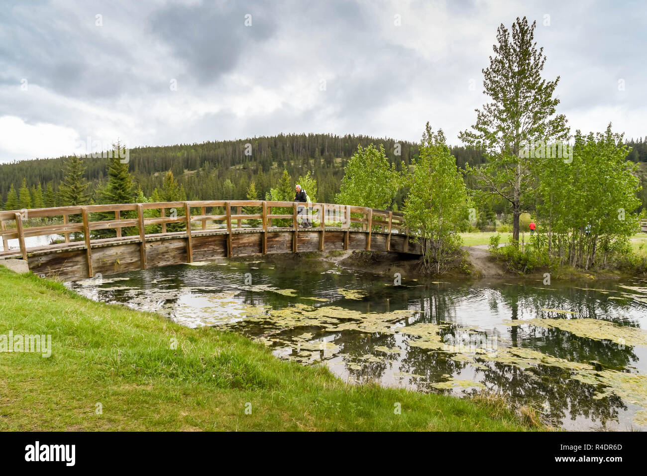 BANFF, AB, CANADA - JUNE 2018: Person crossing a wooden bridge over a ...