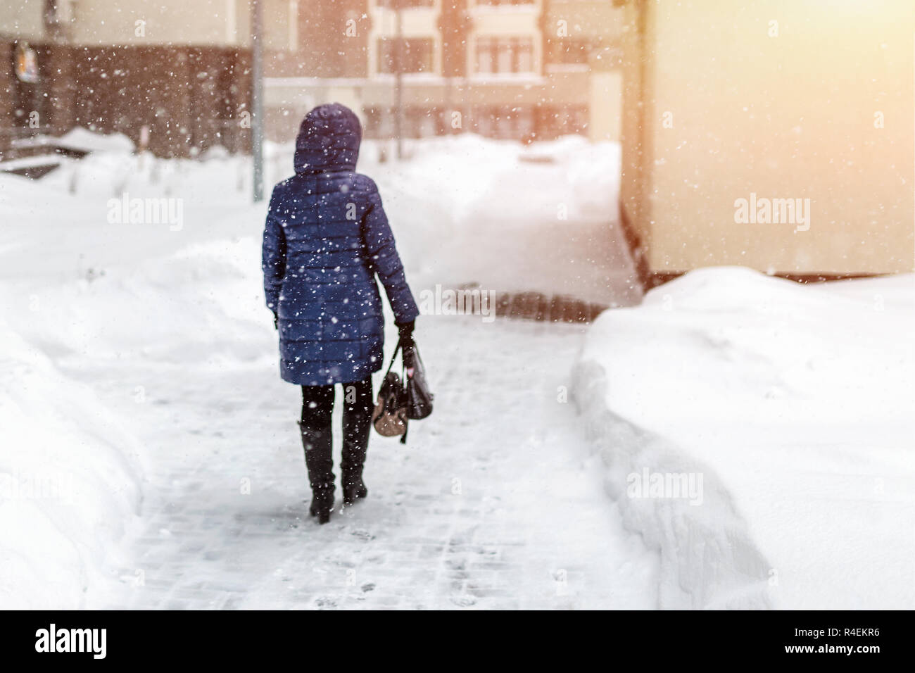 Back of woman in dawn jacket walking through city street during heavy ...