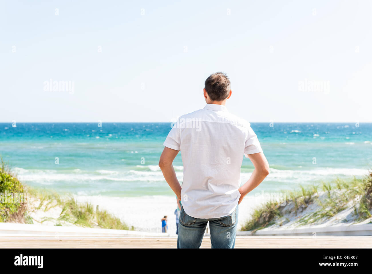 Back of young man standing by beach shore at sunny day in Seaside ...