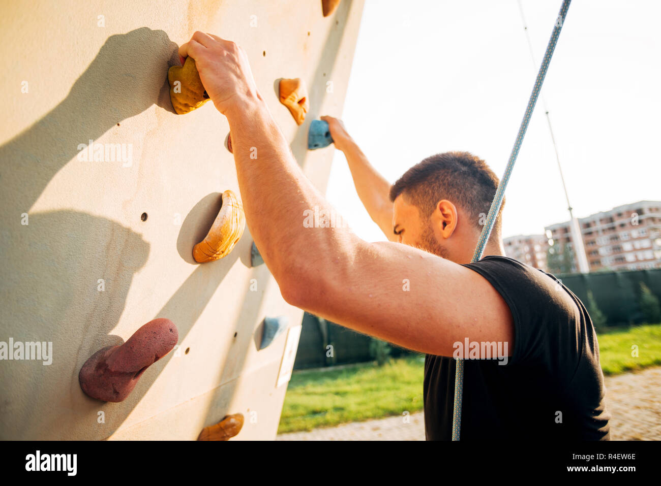 Man wearing belaying rope, climbing on a very high rock climbing wall ...