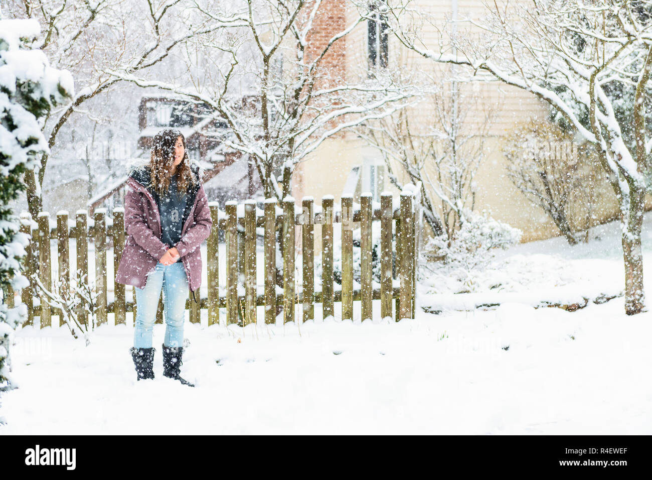 Young woman standing in winter coat in front yard, backyard with ...