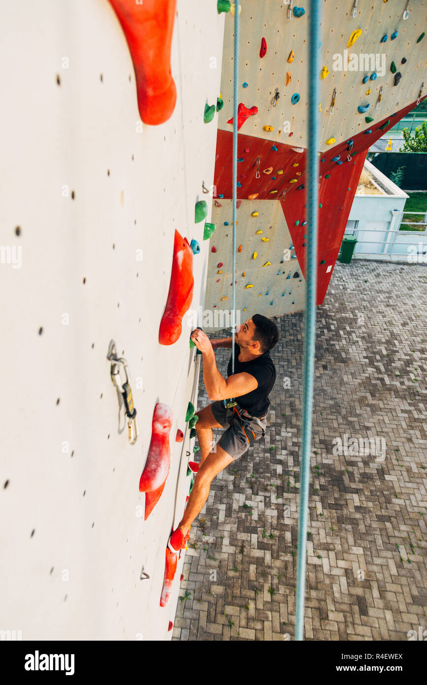 Man wearing belaying rope, climbing on a very high rock climbing wall ...