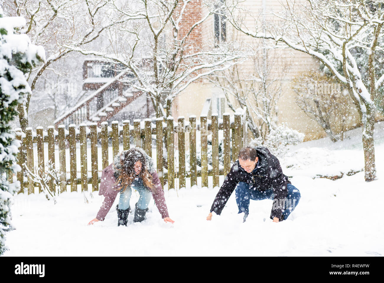 Young man, woman playing, sitting, making snowballs in winter snowstorm ...