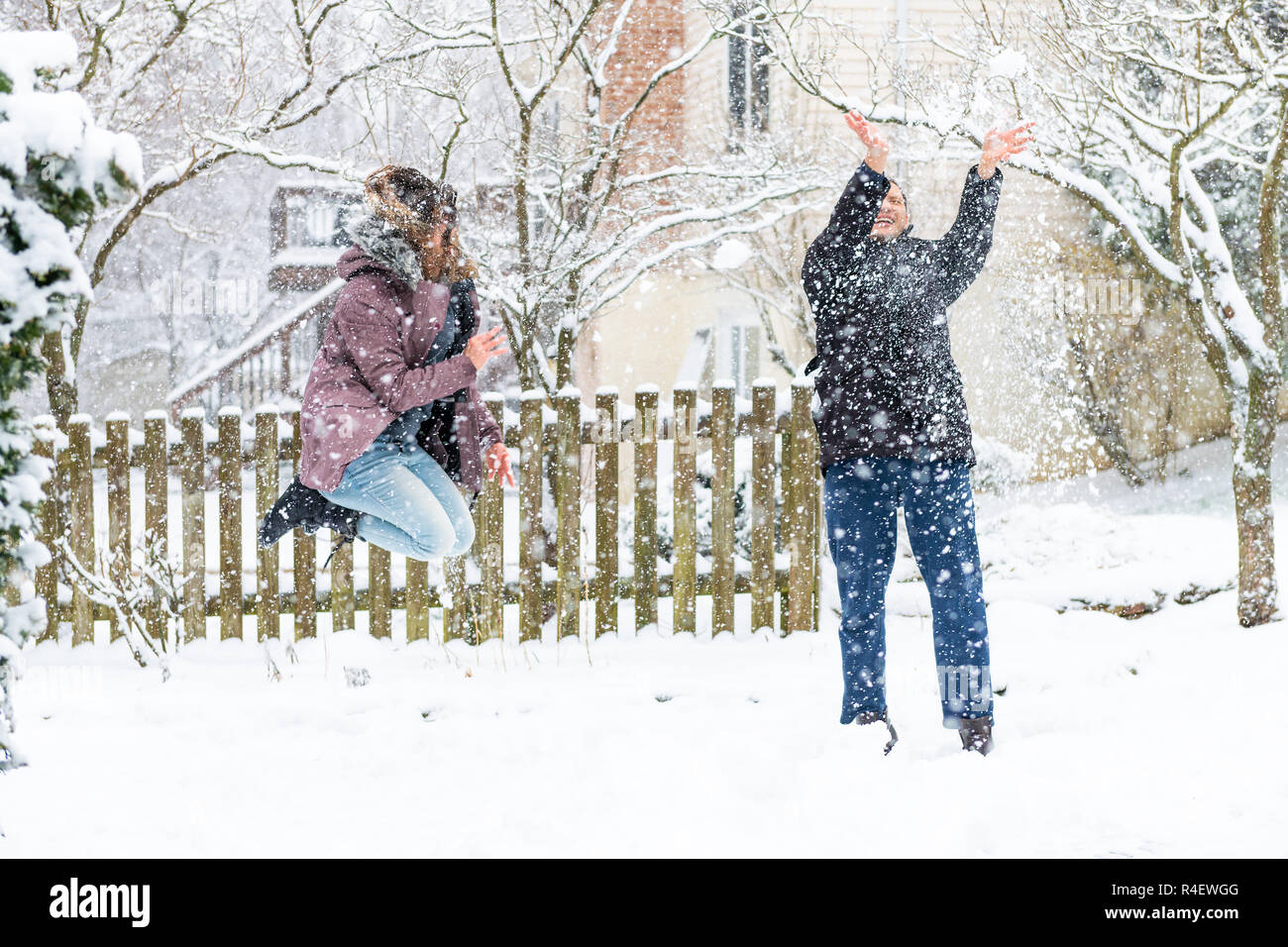 Young woman jumping mid-air, air, playing, throwing snowballs at man in ...