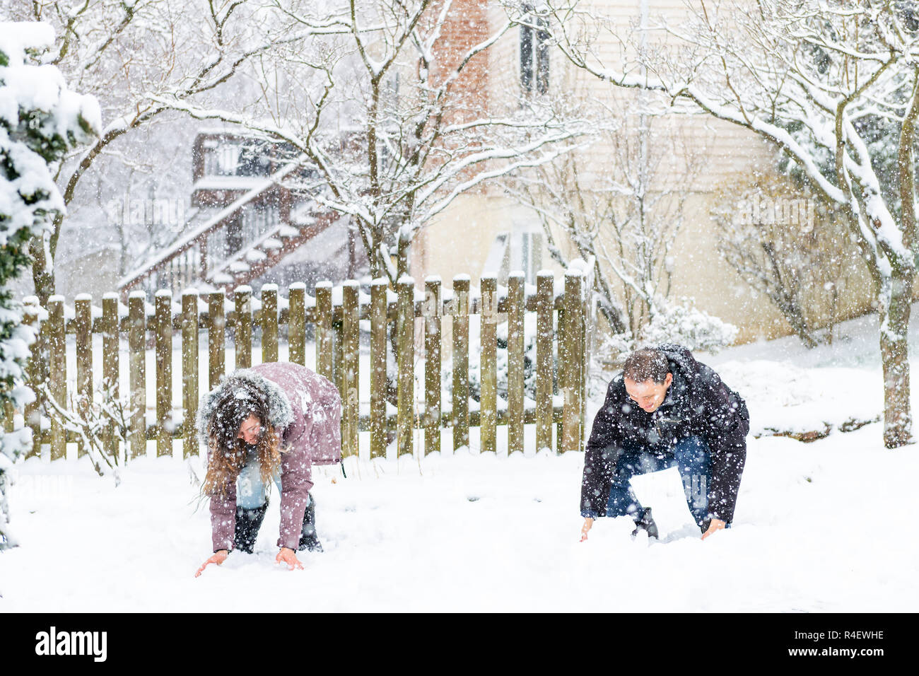 Young woman, man sitting, making snowballs, playing in winter snowstorm ...
