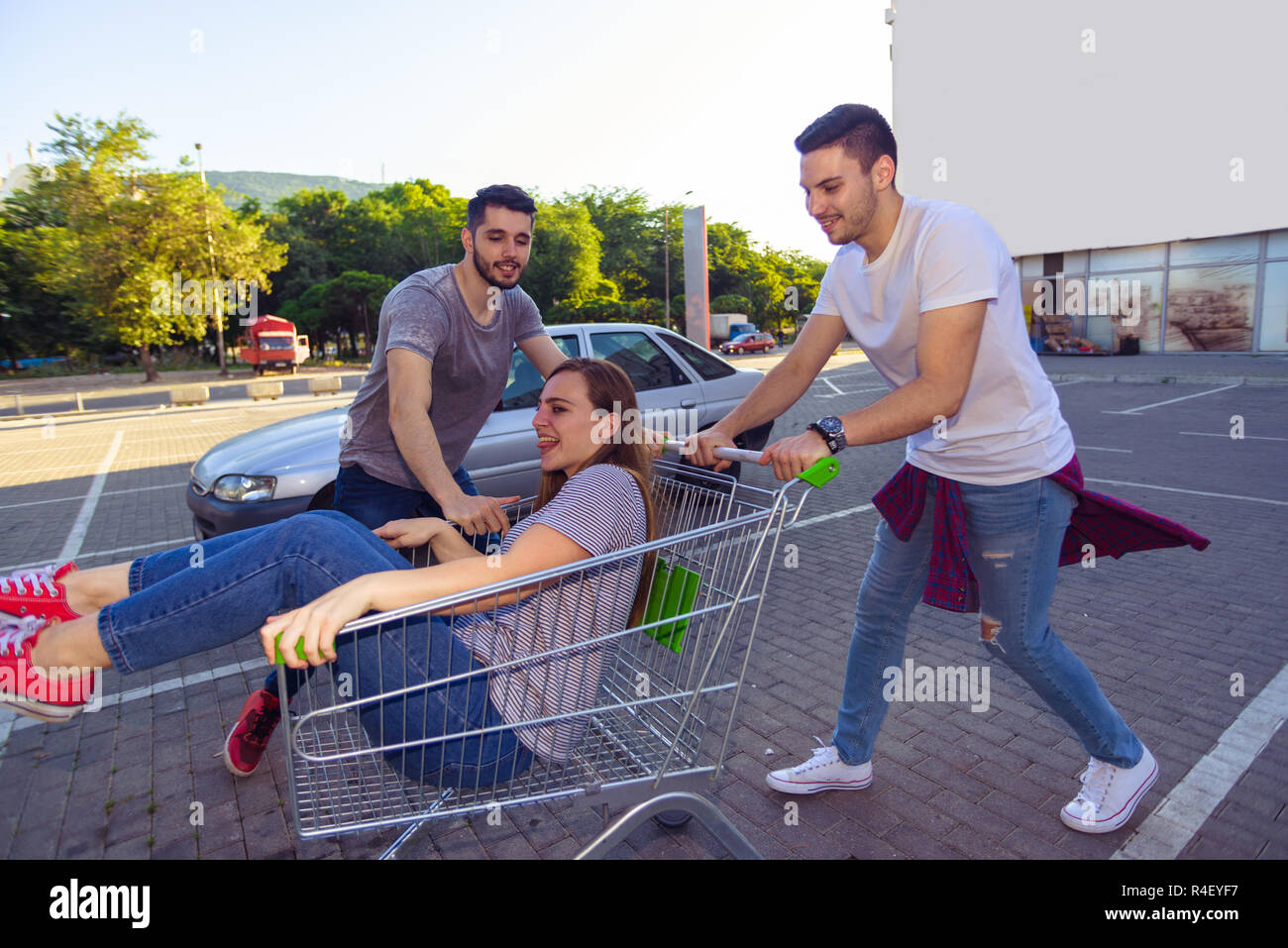 Two laughing young friends pushing their friend down a walkway in the ...