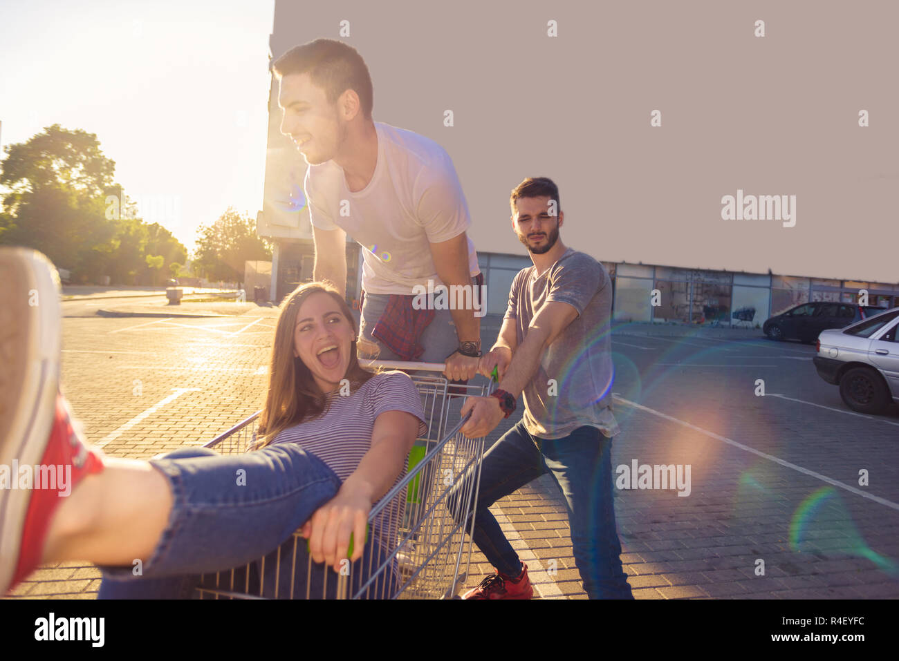 Two laughing young friends pushing their friend down a walkway in the ...