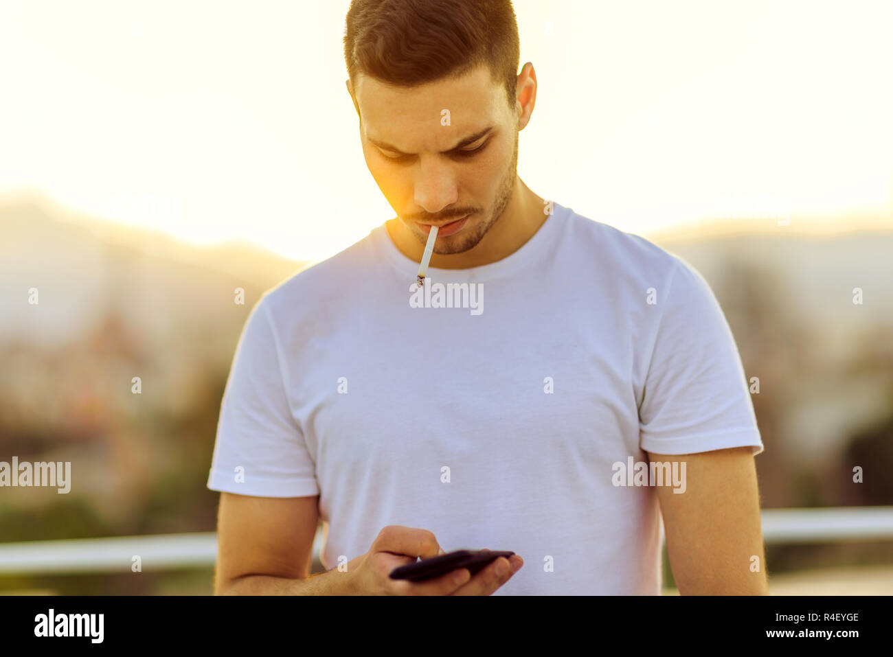 Young man holding his cellphone while smoke cigarette on the balcony in ...