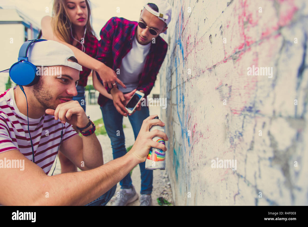 Three young friends having fun while drawing graffiti on the wall with ...