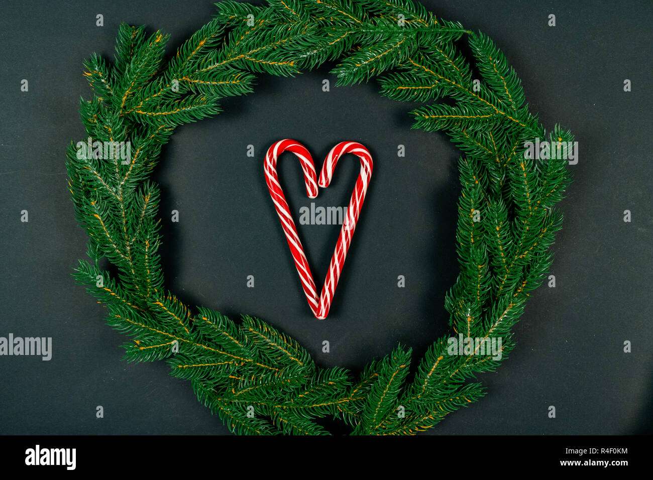 Candy canes in heart shape in the middle of the green wreath made of fir branches on the black ...