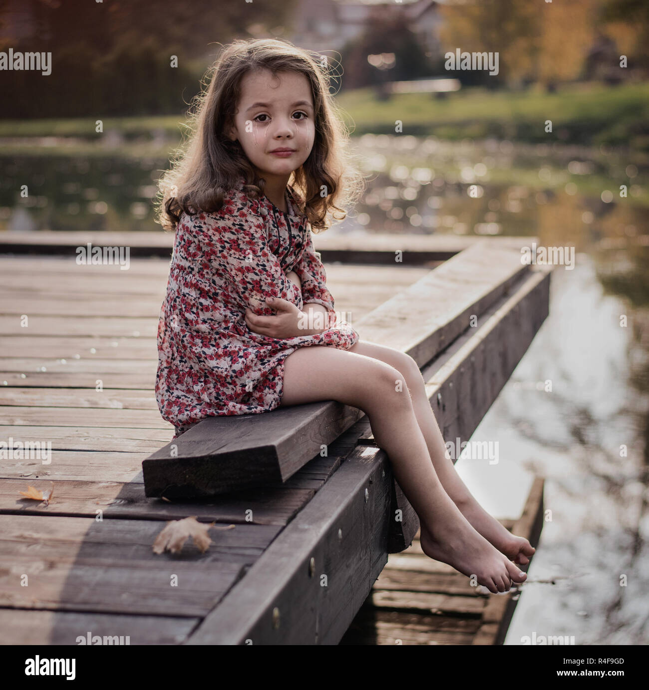 Portrait of a miserable, little girl sitting on a jetty Stock Photo - Alamy