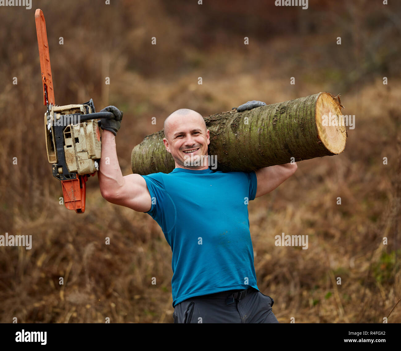 Strong muscular lumberjack with chainsaw, carrying a huge log on his ...