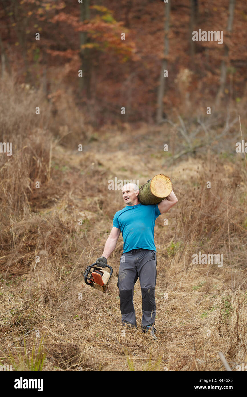 Strong muscular lumberjack with chainsaw, carrying a huge log on his shoulder Stock Photo - Alamy
