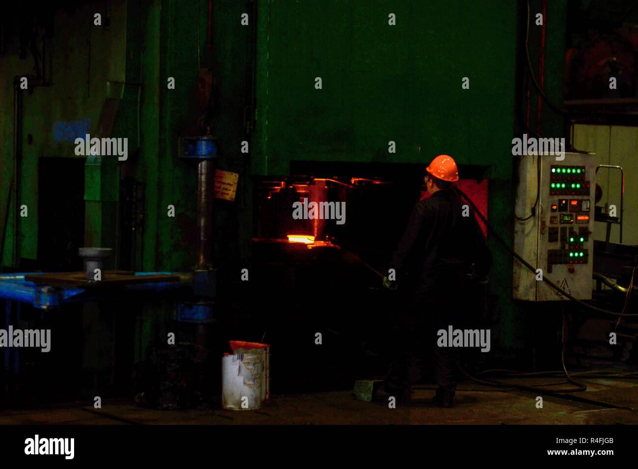 Hot metal ingot being loaded into a hammer forge. Worker forges iron ...