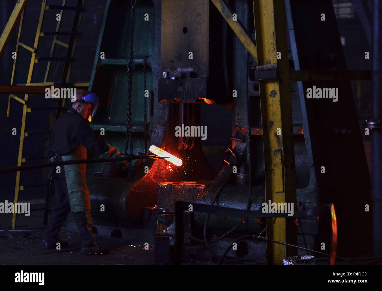 Hot metal ingot being loaded into a hammer forge. Worker forges iron ...