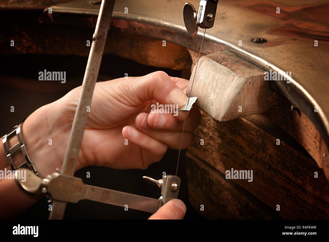 hands of a goldsmith saw a piece of silver on the workbench with a ...