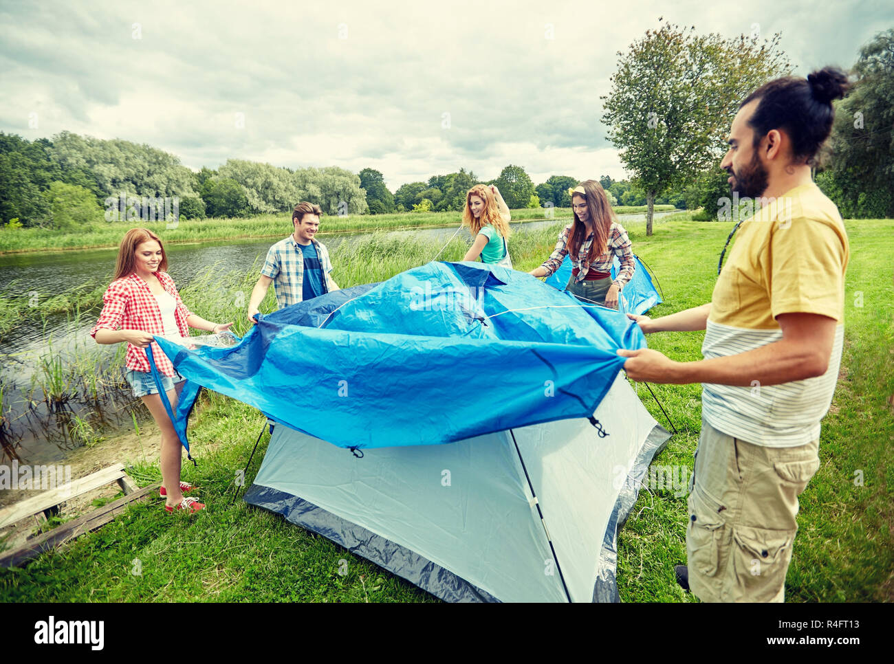 group of smiling friends setting up tent outdoors Stock Photo - Alamy