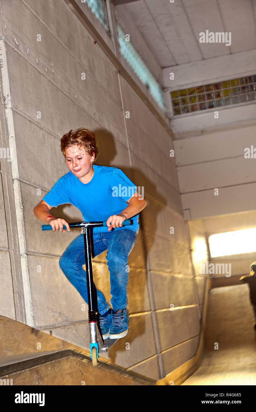 boy jumping with his scooter over a ramp in the skatehall Stock Photo ...
