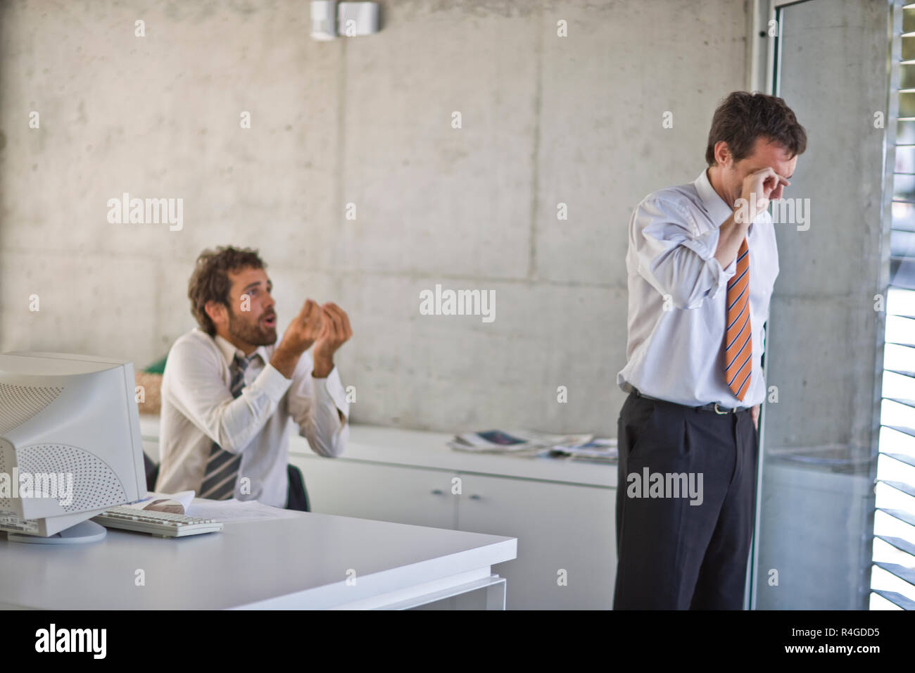 Mid-adult business man crying and rubbing his eyes while his colleague ...