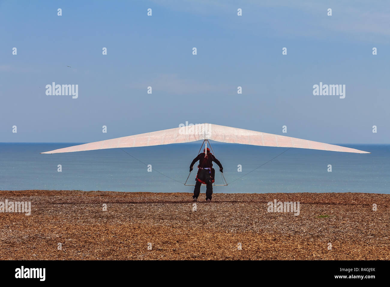 Unidentifiable hang glider on a white wing jumping off a cliff at at ...