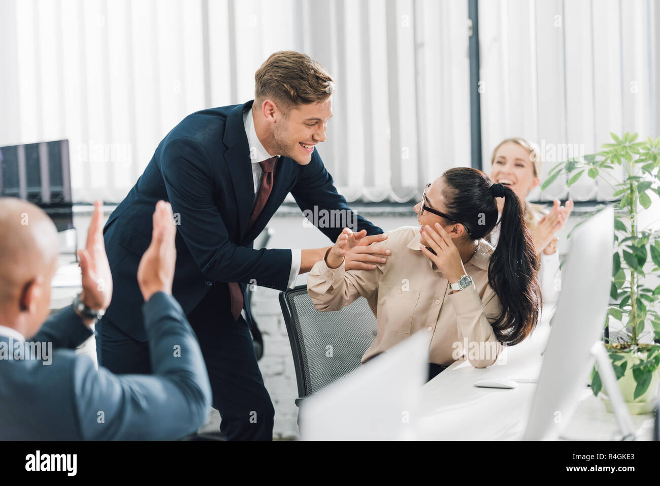 cheerful young business people greeting happy female colleague at workplace Stock Photo - Alamy