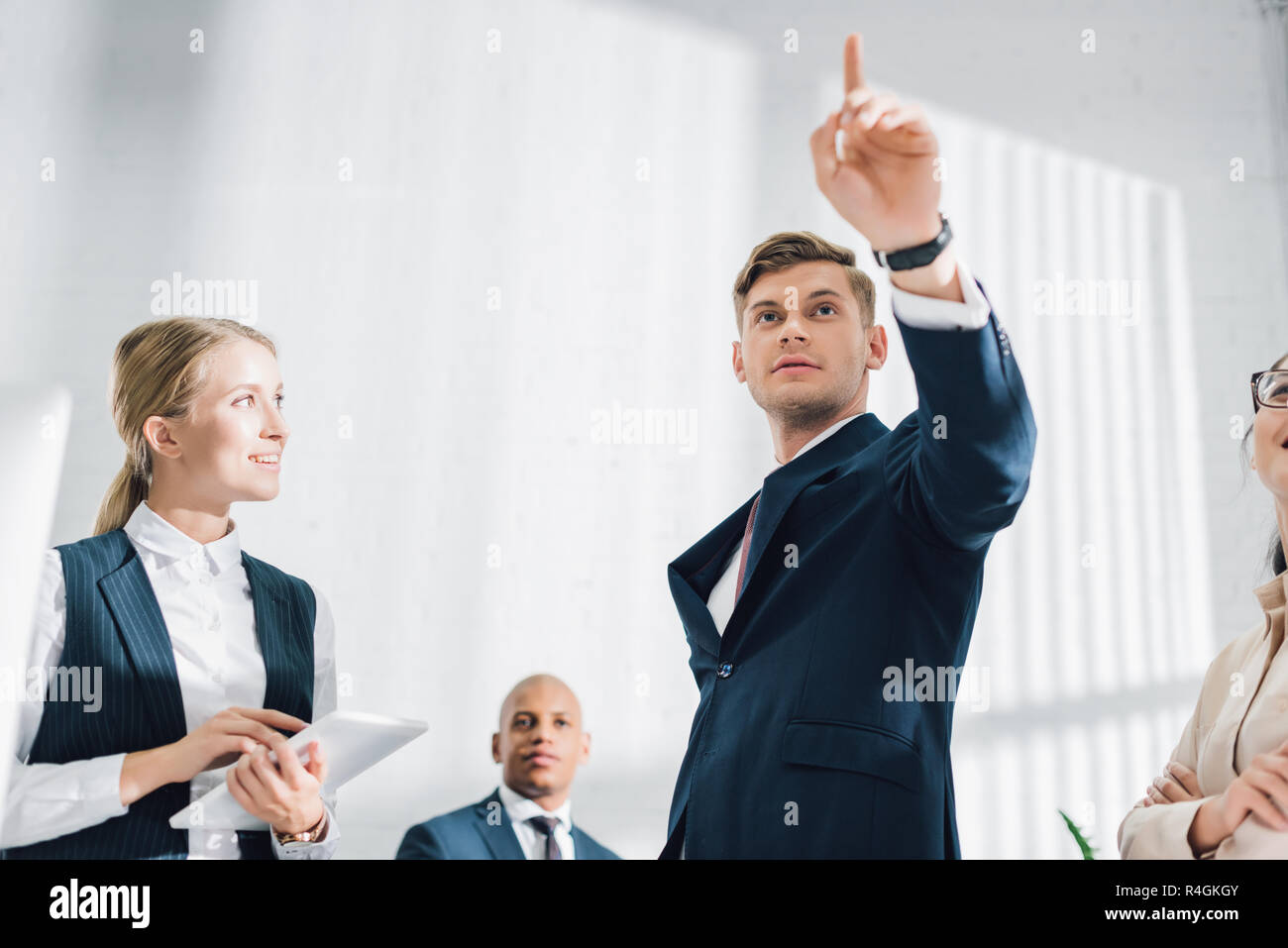 low angle view of coworkers looking at young businessman pointing up ...