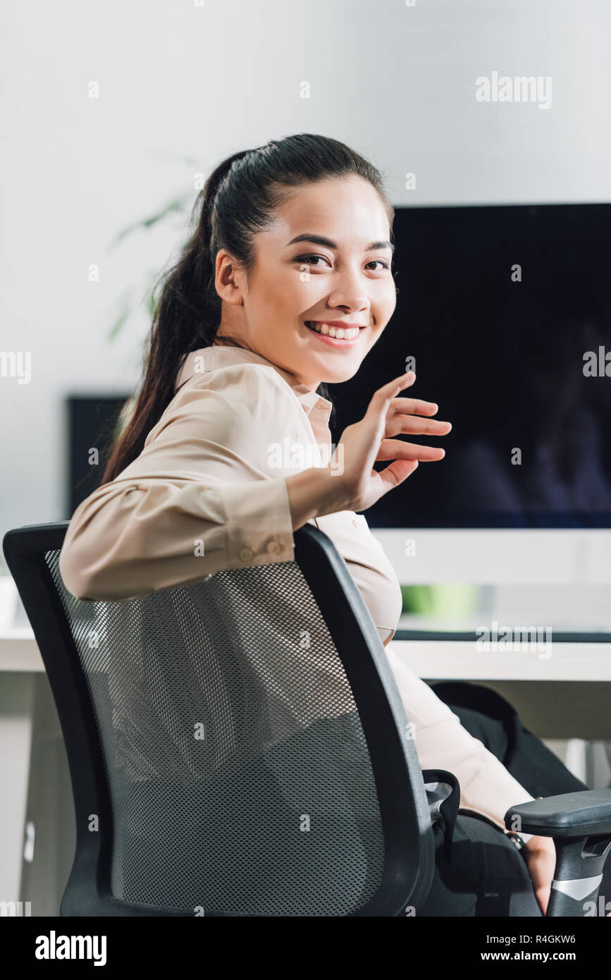 beautiful young businesswoman waving hand and smiling at camera while ...