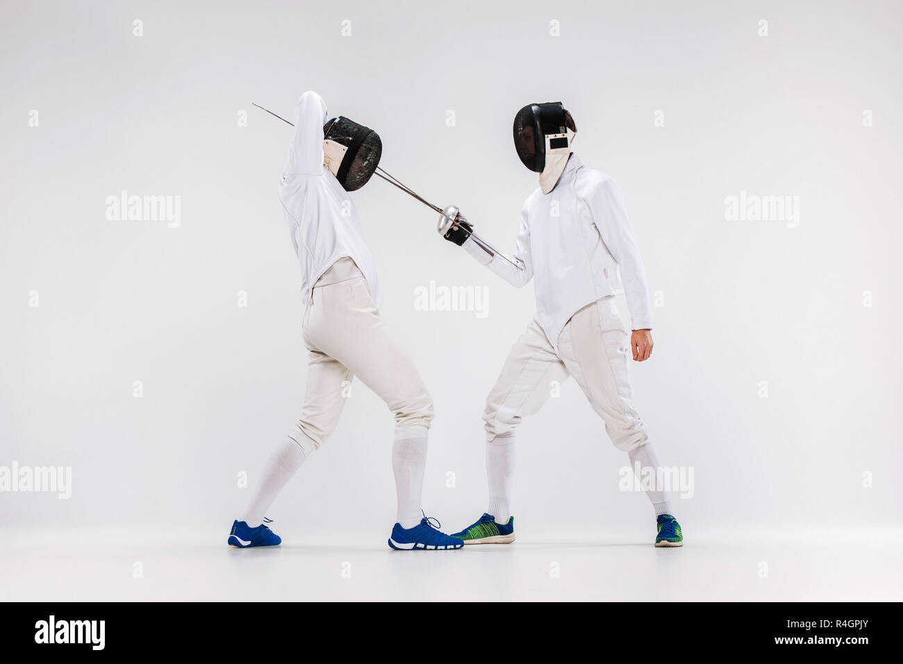 The two men wearing fencing suit practicing with sword against gray ...