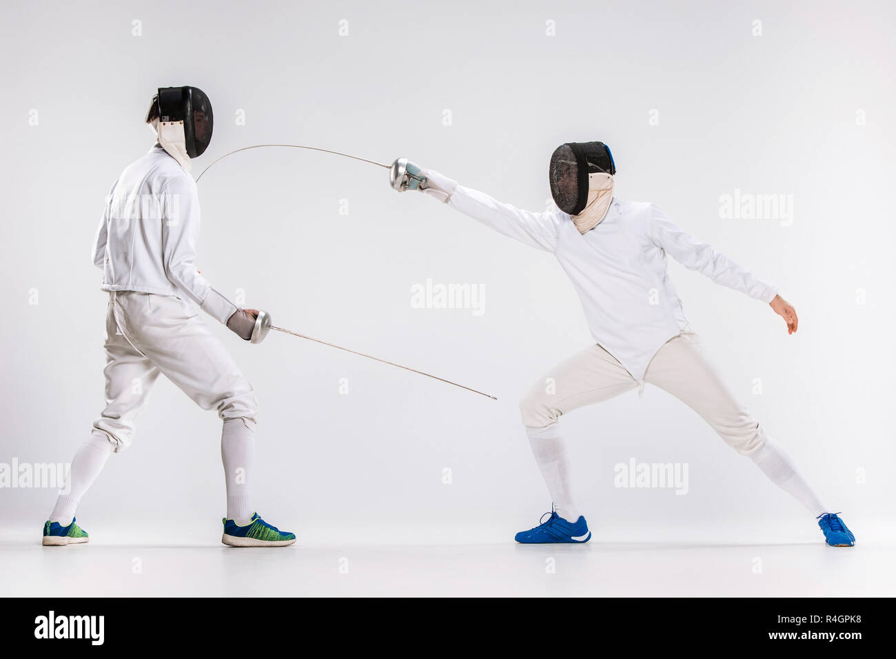 The two men wearing fencing suit practicing with sword against gray ...