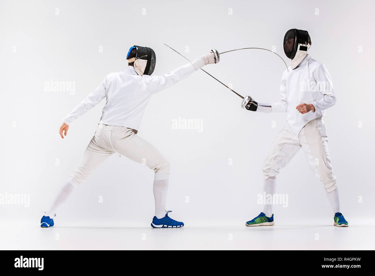The two men wearing fencing suit practicing with sword against gray ...