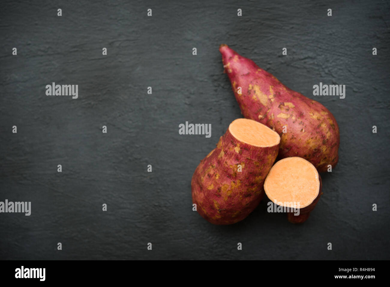 Raw orange sweet potatoes close up on dark background. Copy space top ...