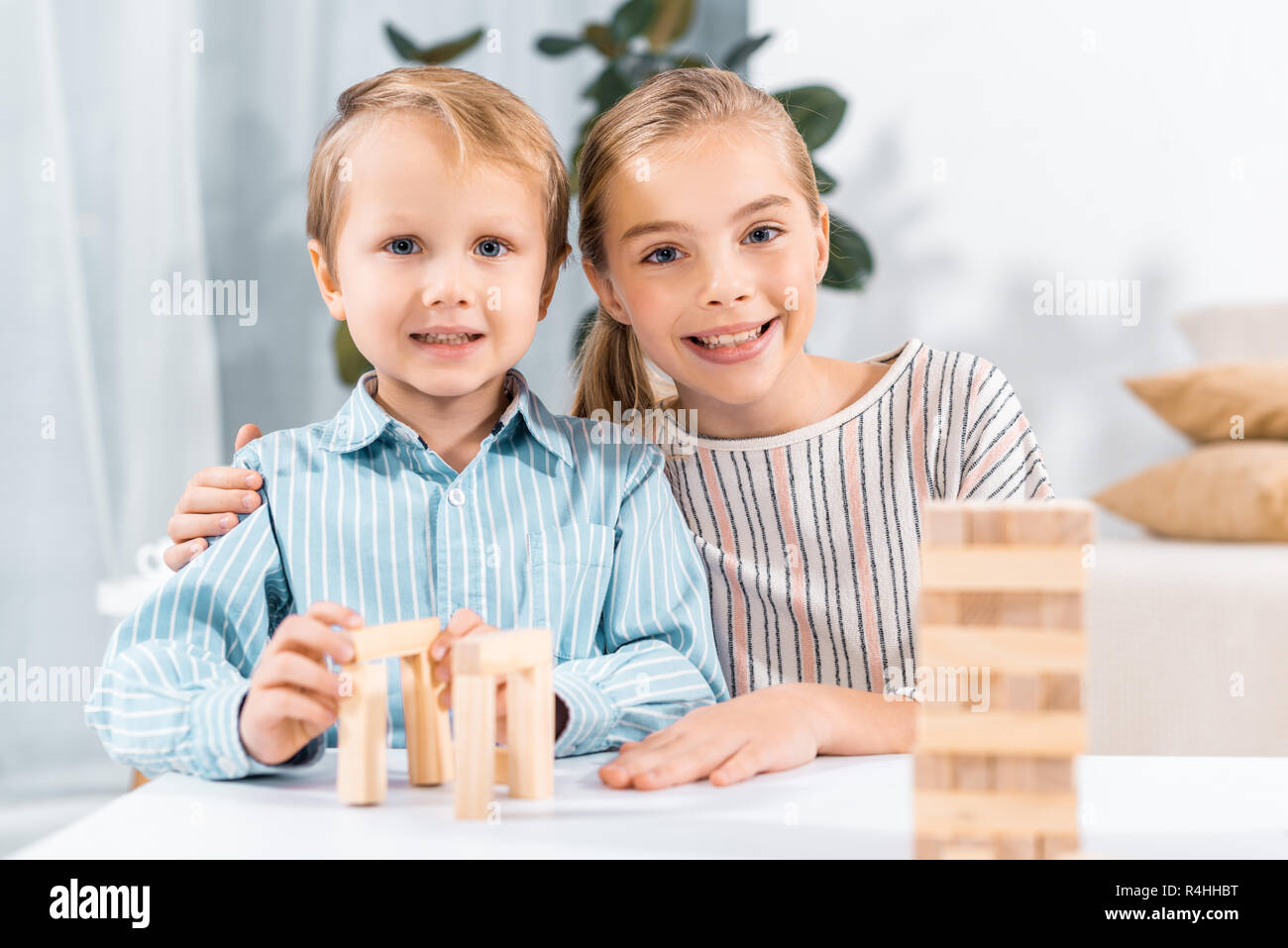 portrait of smiling child embracing little brother at table with blocks ...