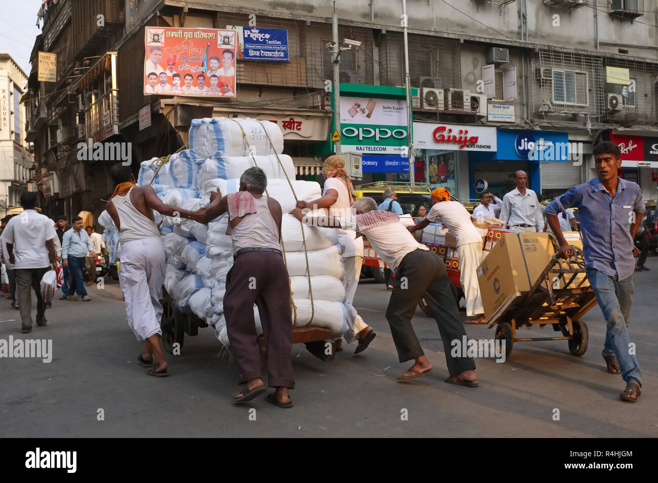 Porters push or pull carts laden with goods through Kalbadevi Road ...