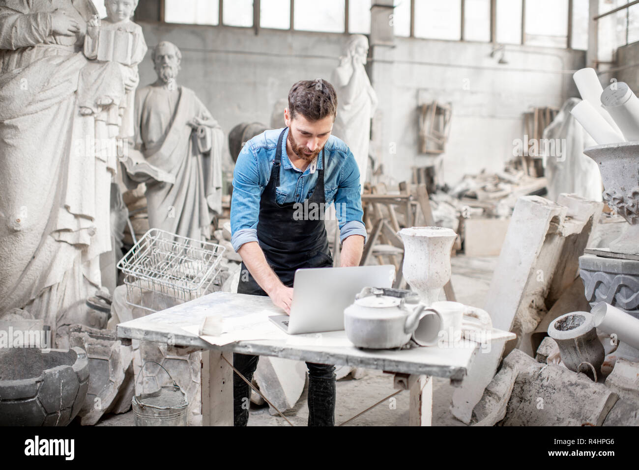 Handsome sculptor working with laptop at the working place in the old ...