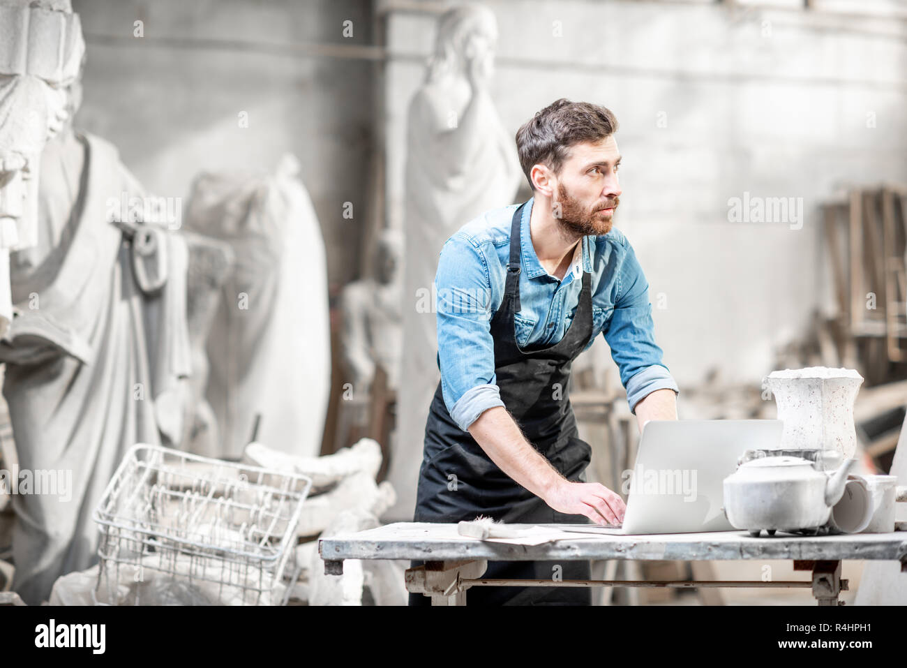 Handsome sculptor working with laptop at the working place in the old ...