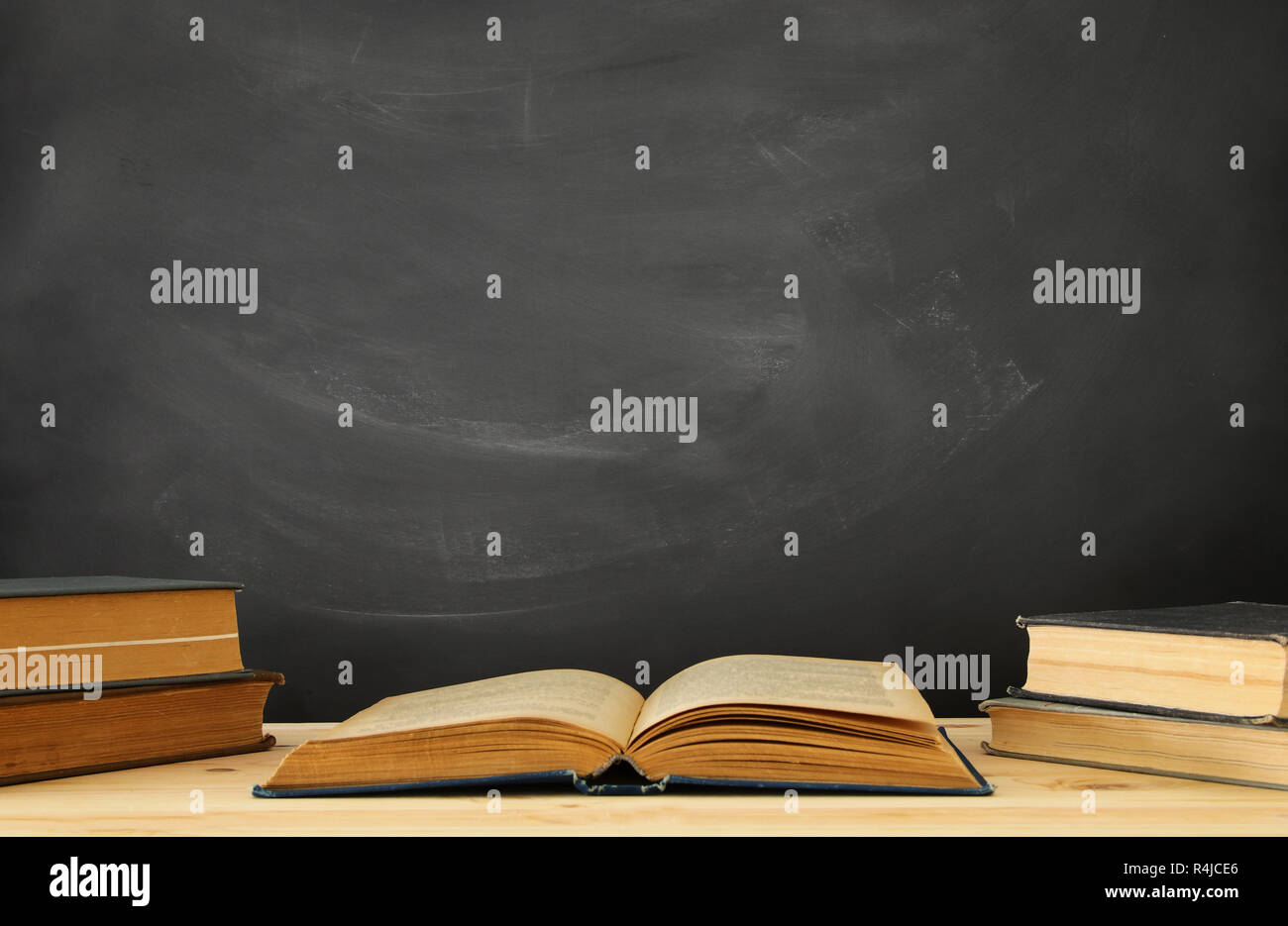 stack of books over wooden desk in front of blackboard Stock Photo - Alamy