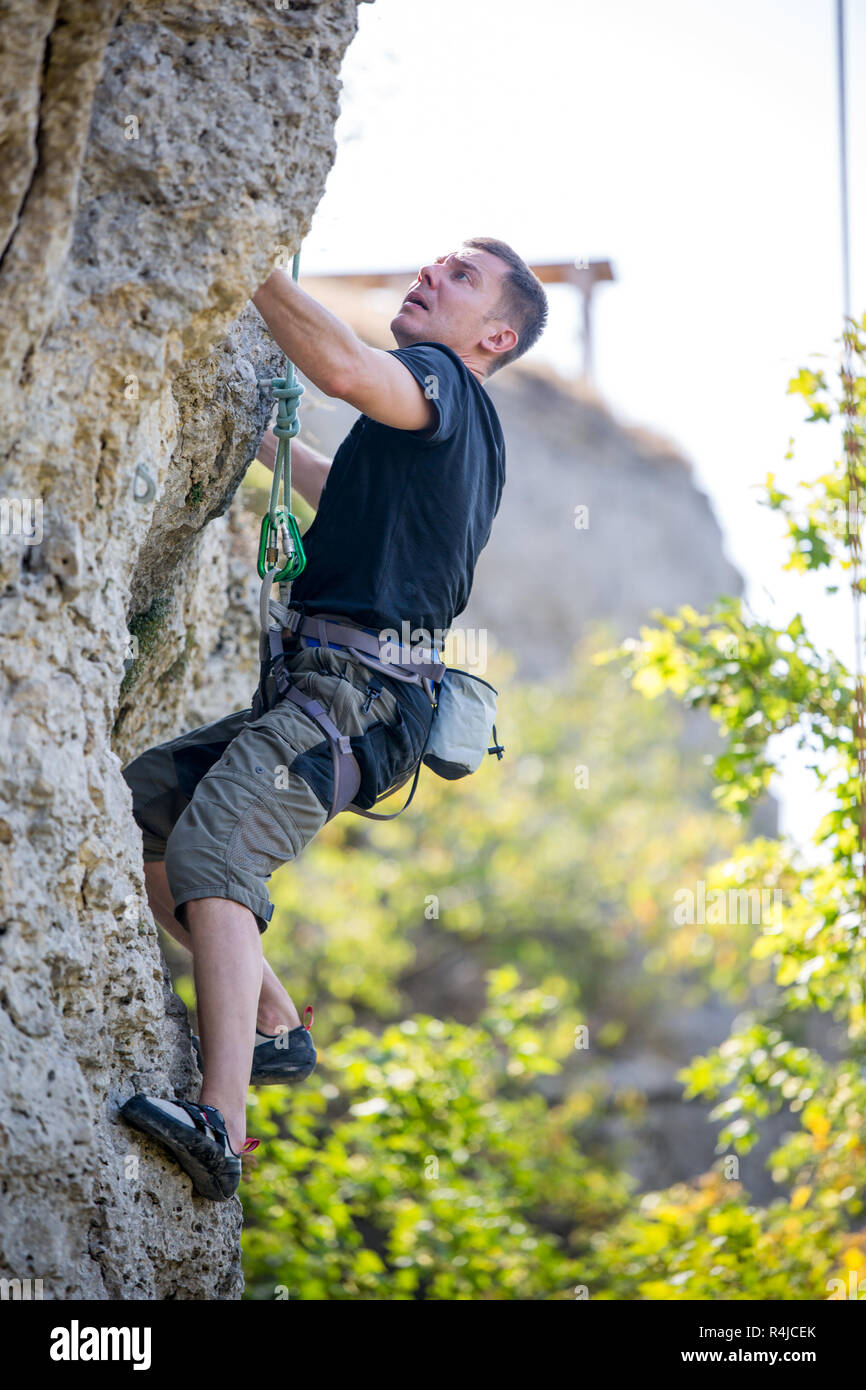 Photo of athlete man in helmet clambering over rock against background ...