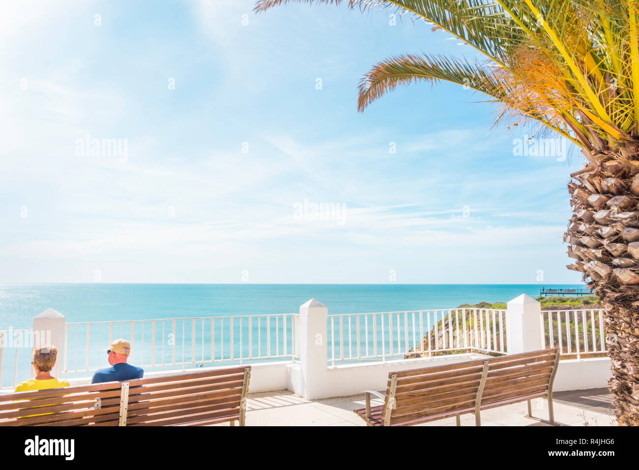 couple seated on a bench at seafront promenade, albufeira, algarve ...