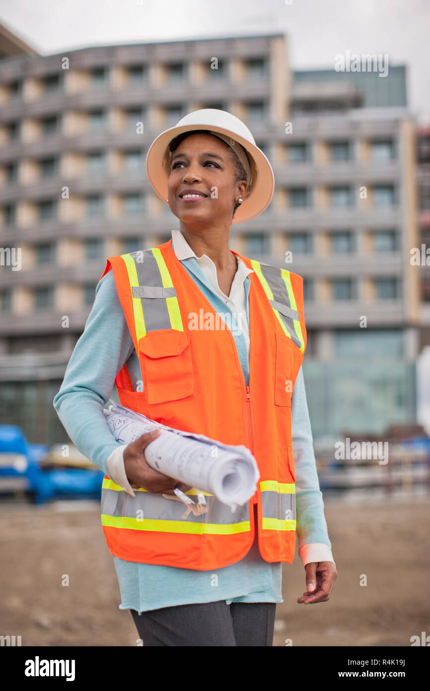 Proud young female engineer holding a roll of building plans on a ...