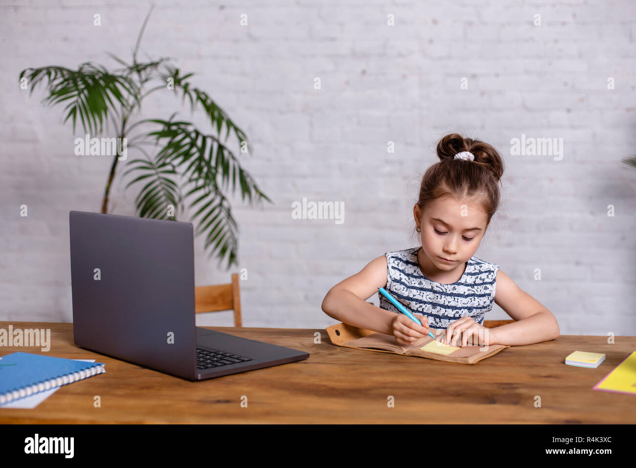 Cute little girl is sitting at table with her laptop and notebook. The ...