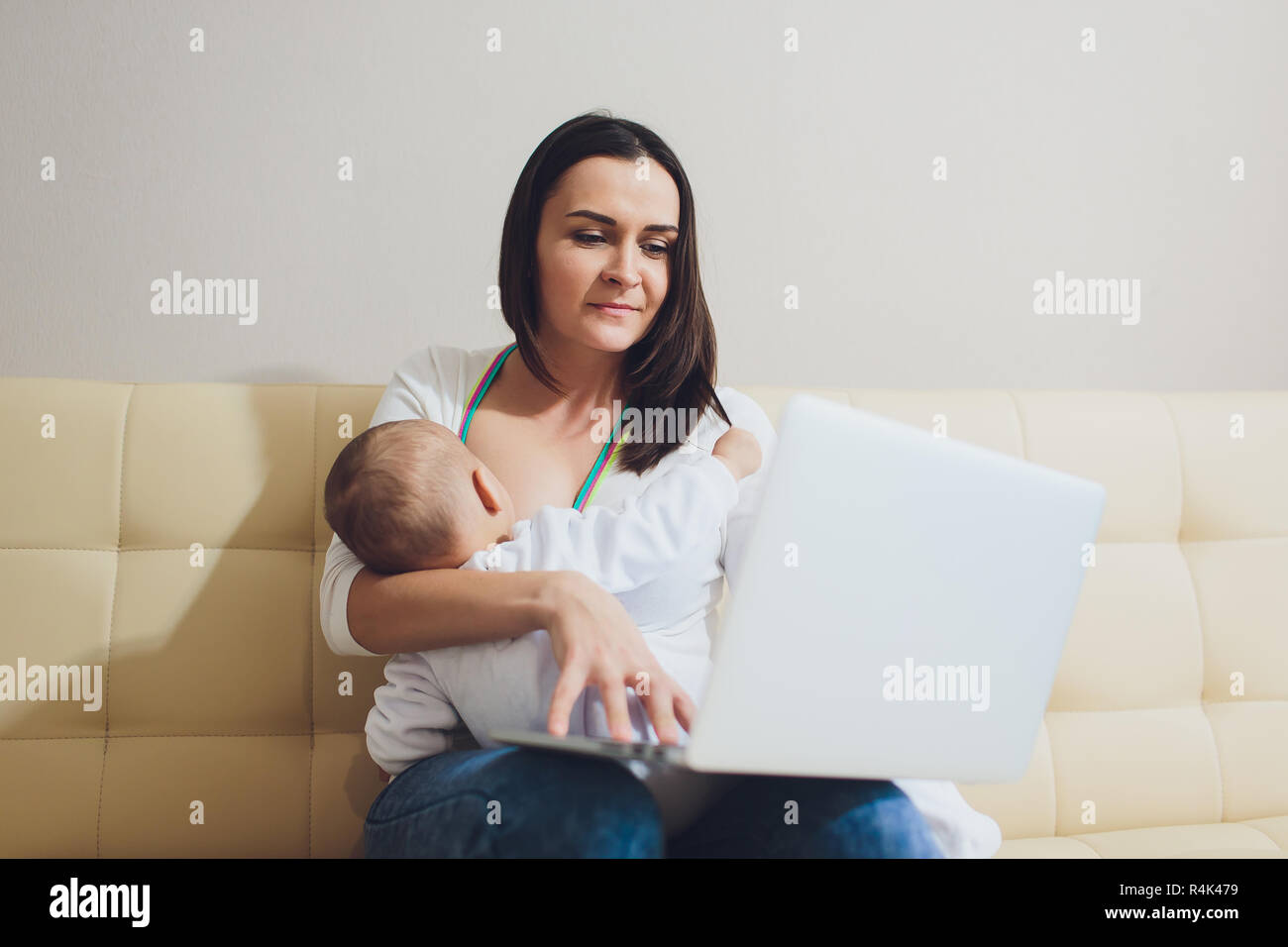 Beautiful young mother working with laptop computer and breastfeeding ...