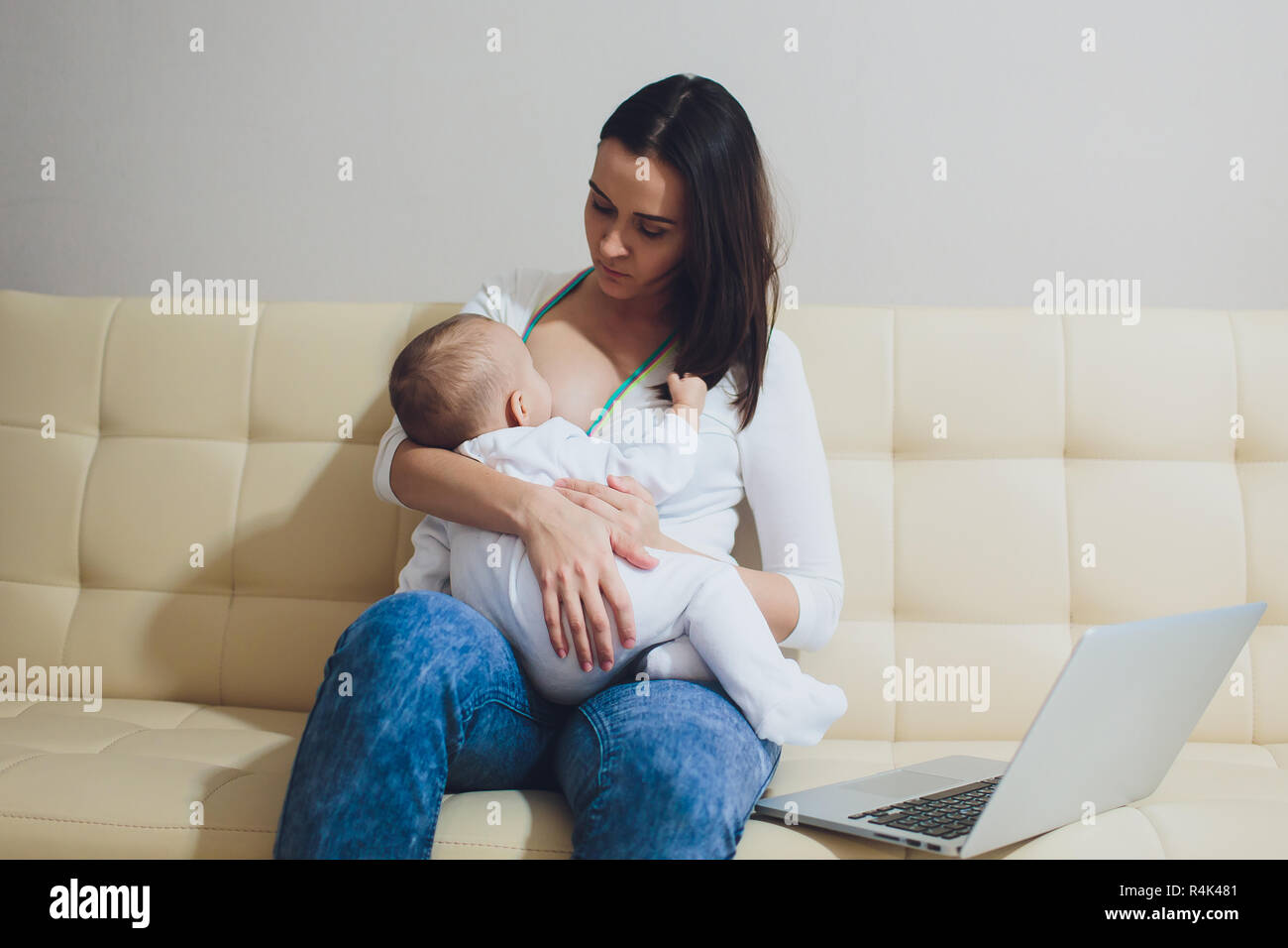 Beautiful young mother working with laptop computer and breastfeeding ...