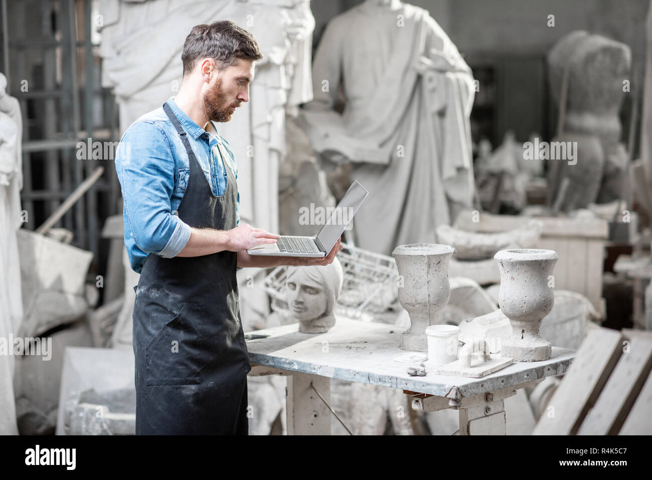 Handsome sculptor working with laptop in the atmospheric studio with ...