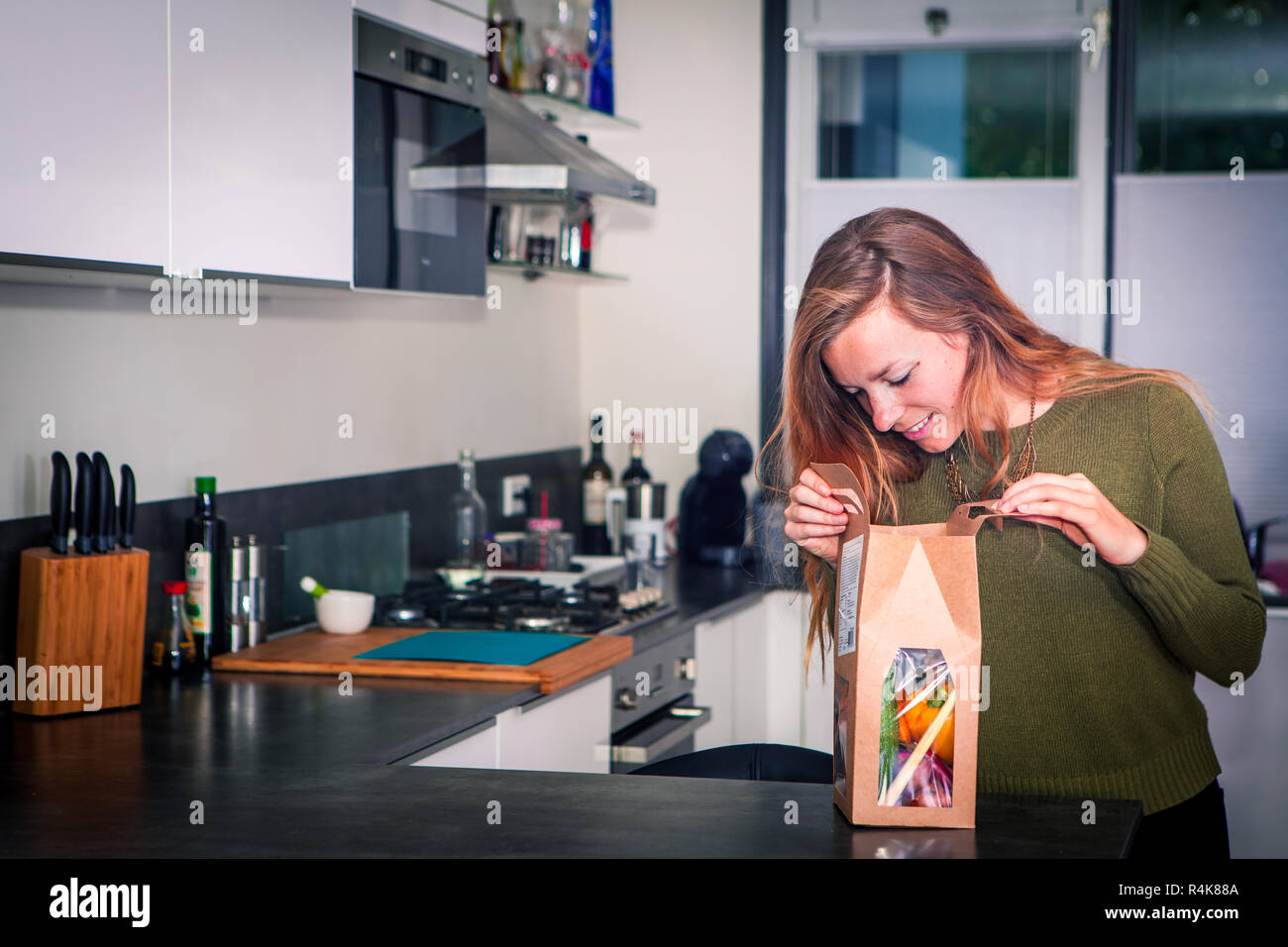 Young woman opens a package of fresh ingredients for healthy dinner ...