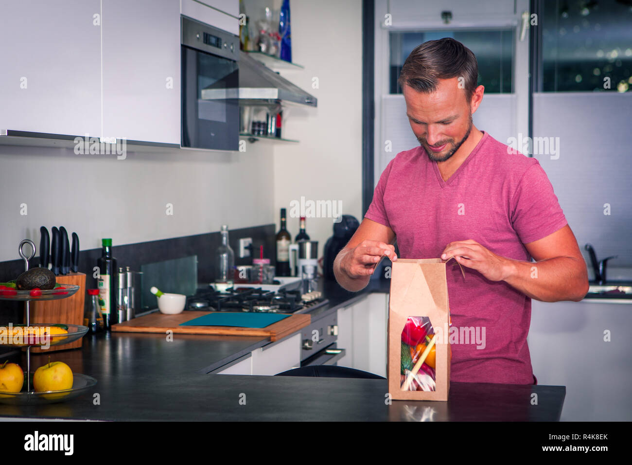 Young man opens a package of fresh ingredients to make a healthy dinner ...
